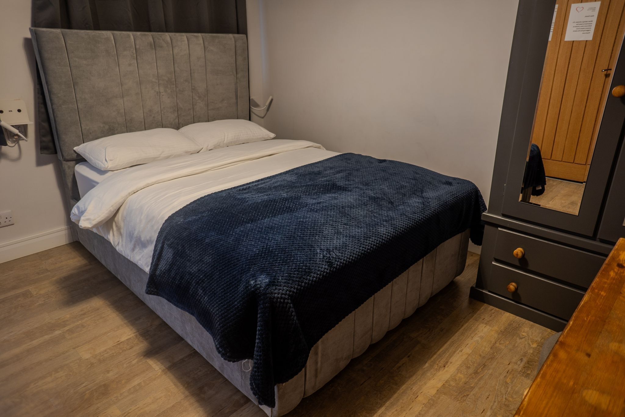 Quarto com cama, guarda-roupa de madeira e espelho.