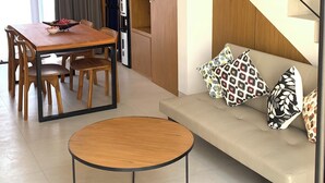Uma sala de estar moderna com um sofá, uma mesa de jantar e cadeiras. Há uma escada com corrimão e uma estante embutida acima.