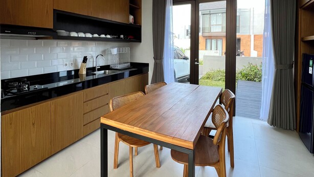 Uma cozinha moderna com armários de madeira, bancada preta e um espaço de refeições com mesa e cadeiras de madeira.