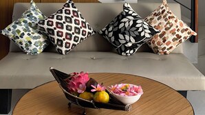 Uma sala de estar moderna com escada, mesa de centro redonda de madeira e sofá com almofadas estampadas.