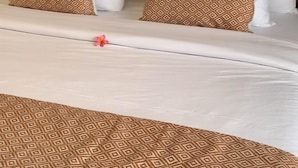 Cama bem arrumada com almofadas brancas e estampadas, cabeceira de madeira e decoração floral visível.