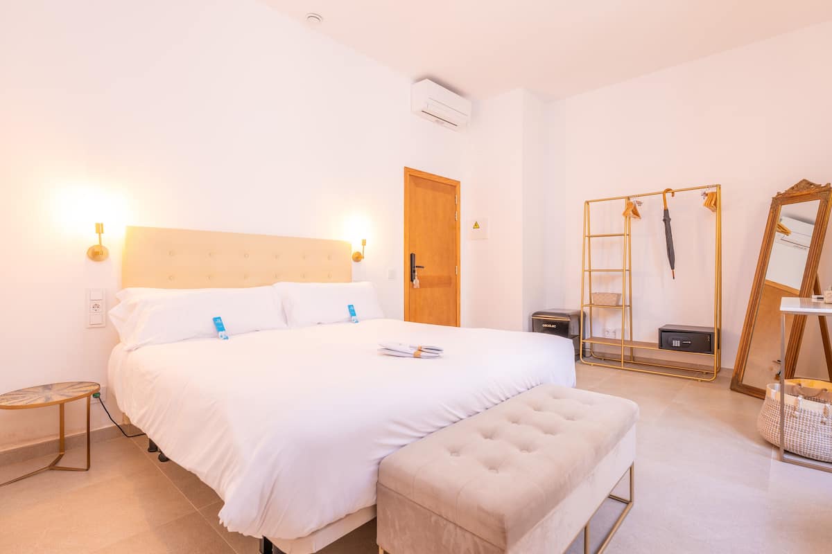 Quarto de hotel com uma cama grande, mesas de cabeceira, um banco, um guarda-roupa e um espelho.
