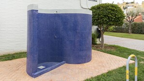 Área de chuveiro ao ar livre com azulejos azuis, adjacente a um edifício branco.
