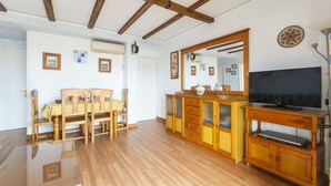 Um quarto espaçoso com piso de madeira, uma mesa de jantar com cadeiras, um armário de madeira com uma televisão e um espelho grande.