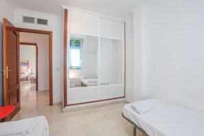 Quarto de hotel com uma grande porta deslizante, uma cama, uma mesinha e vista para outro quarto com cama e mesa de cabeceira.