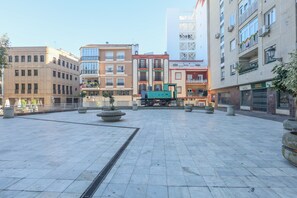 Uma praça ampla com uma grelha de drenagem central, rodeada por edifícios altos com varandas e janelas.