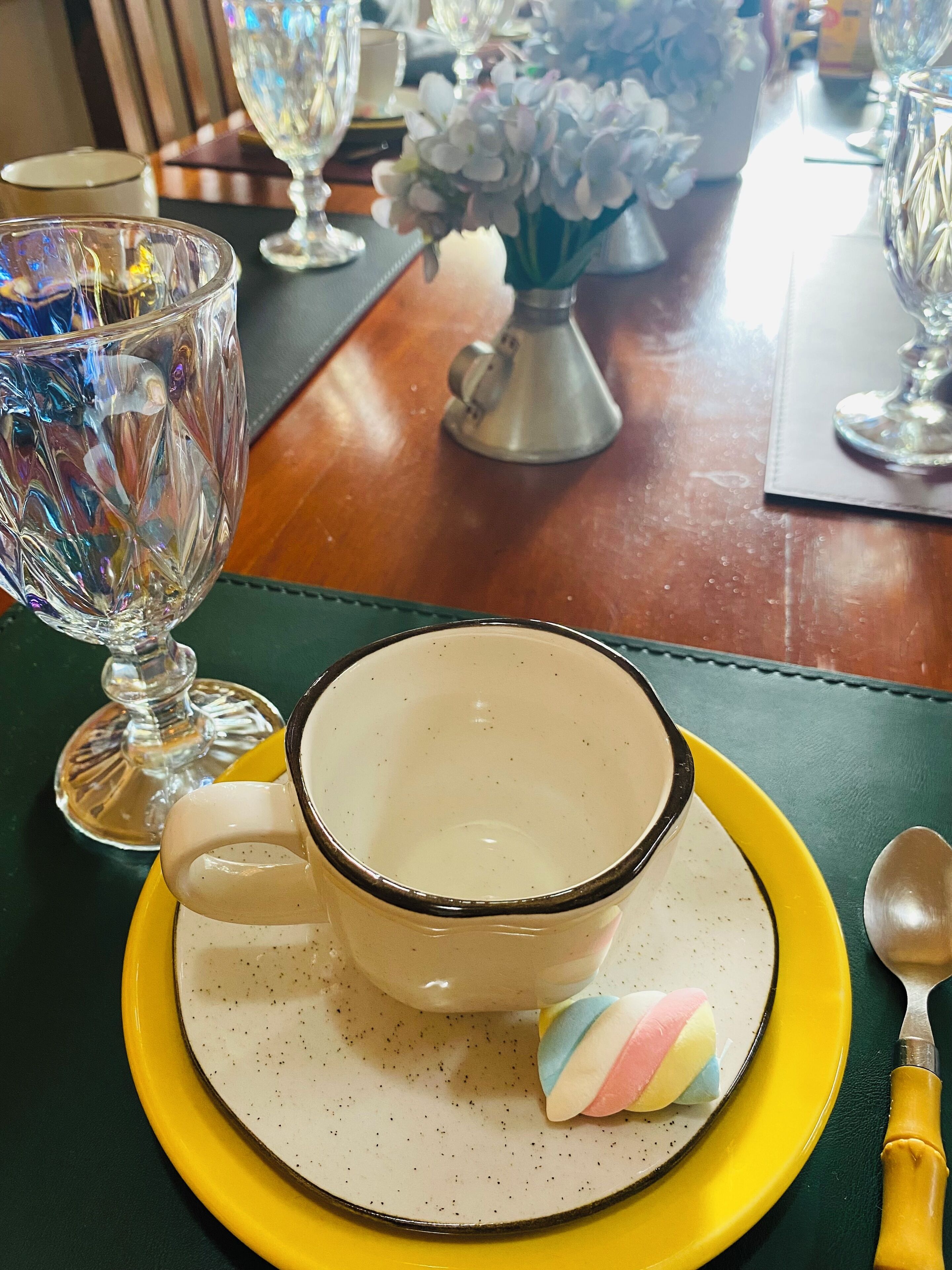 Uma mesa posta com uma caneca branca sobre um prato amarelo, um brinquedo colorido e uma colher.