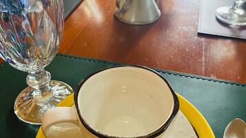 Uma mesa posta com uma caneca branca sobre um prato amarelo, um brinquedo colorido e uma colher.