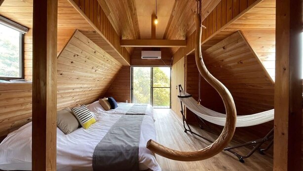 Quarto de cabana de madeira acolhedor, com uma cama grande, uma rede e um candeeiro suspenso.