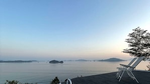 Uma banheira de hidromassagem em um deck de madeira com vista para um mar calmo e ilhas ao longe.