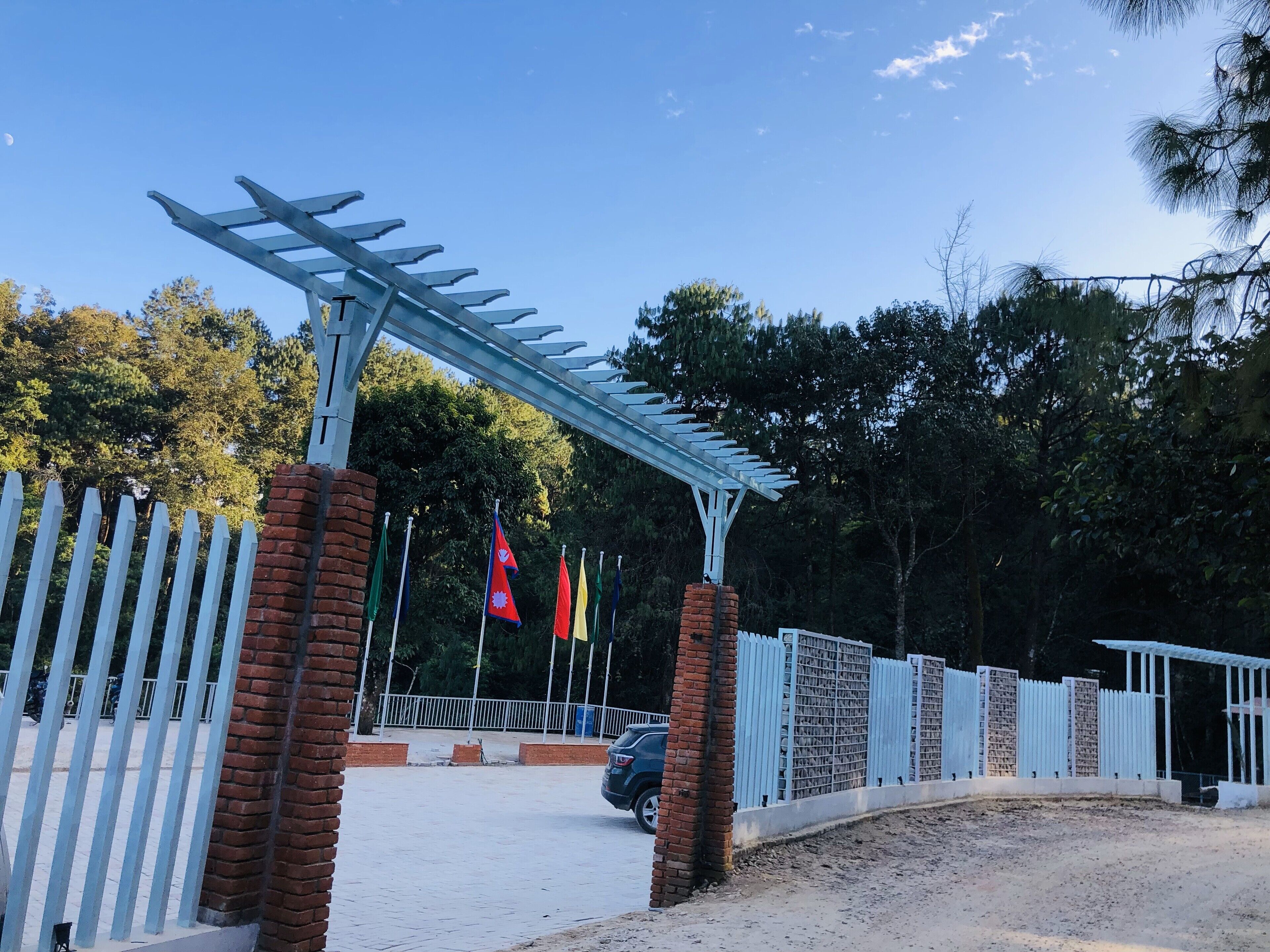 Uma entrada fechada com pérgola, pilares de tijolo e bandeiras.