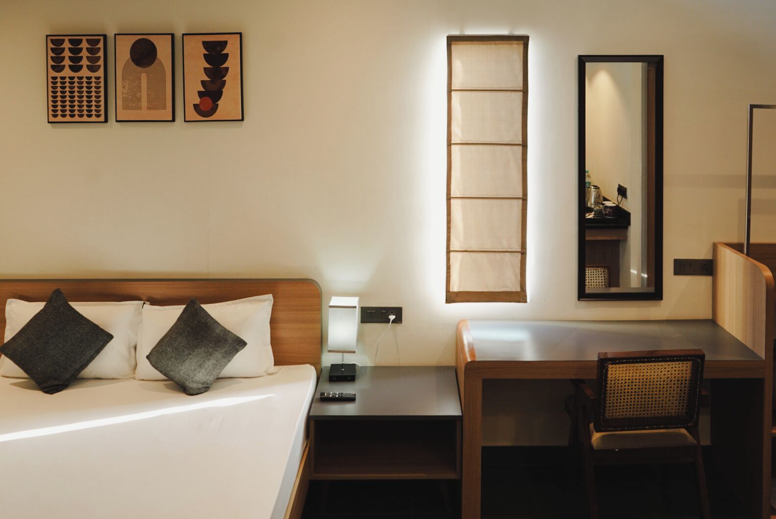 Quarto de hotel com cama, mesa de cabeceira, escrivaninha, cadeira e um espelho grande.