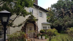 Uma casa de dois andares com um portal de pedra, um pequeno alpendre e um jardim com vasos de plantas.