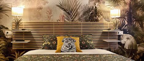 Quarto com cama, mesa de cabeceira, abajur e um mural na parede com uma floresta tropical.