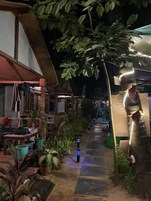 Uma trilha externa com vasos de plantas e uma estrutura de madeira com uma placa.