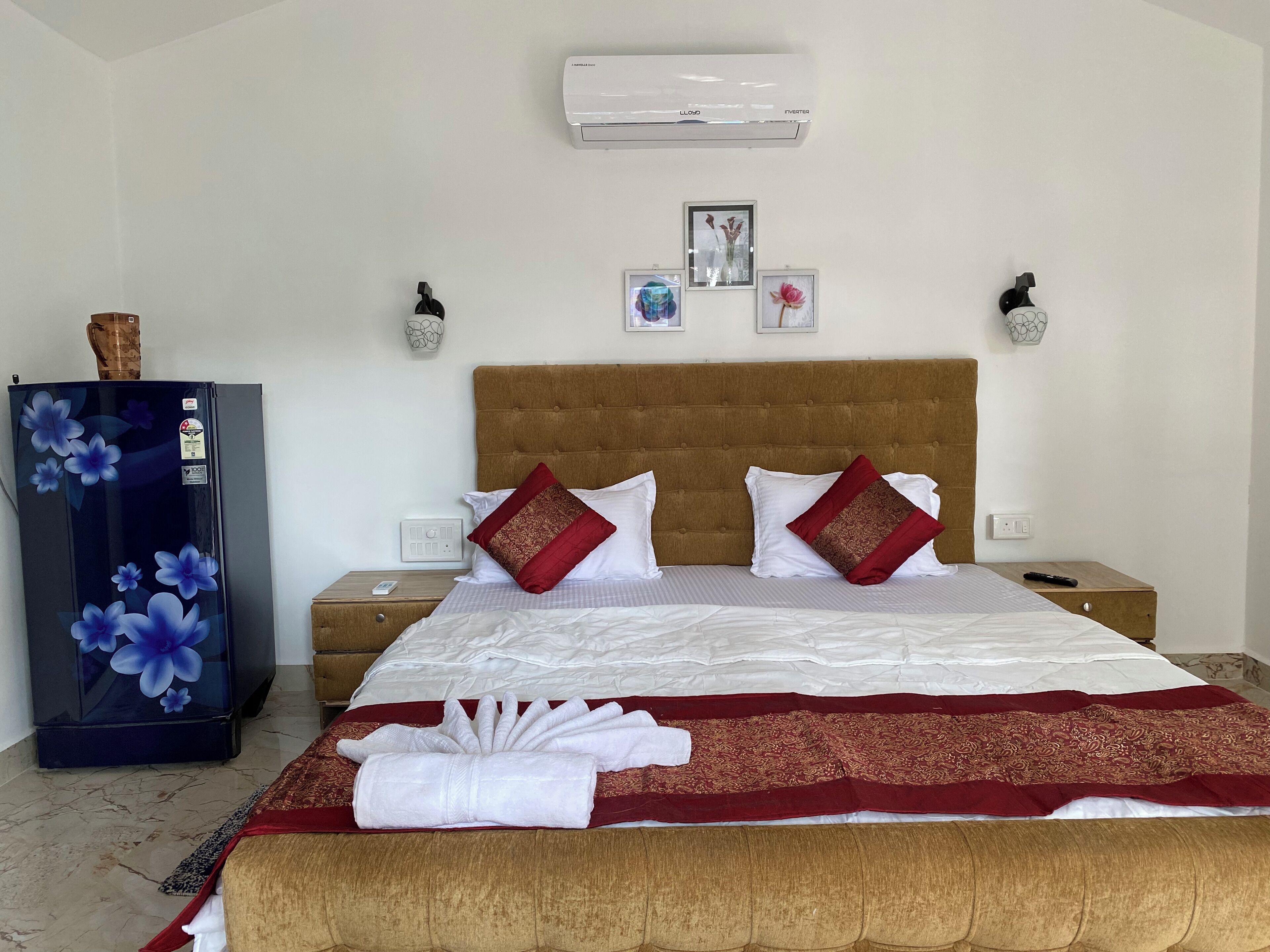 Quarto de hotel com uma cama, mesa de cabeceira, ar condicionado fixado na parede e um frigorífico com motivos florais.