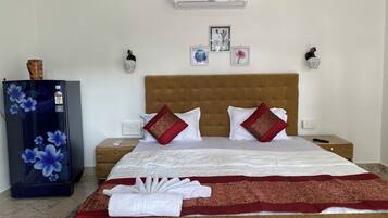 Quarto de hotel com uma cama, mesa de cabeceira, ar condicionado fixado na parede e um frigorífico com motivos florais.