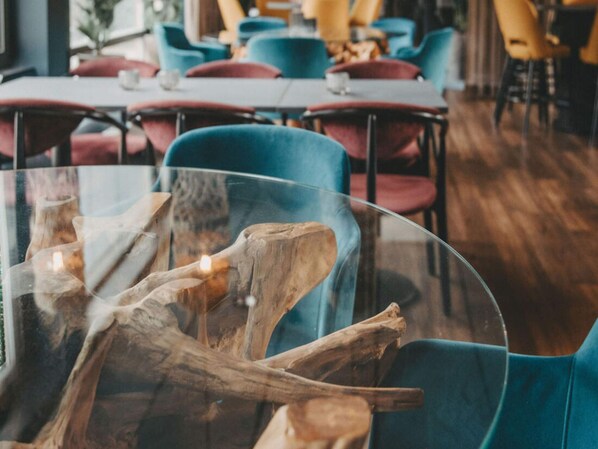 Interior de restaurante com mesas redondas, cadeiras azuis e mesa de vidro com um centro de mesa de madeira.