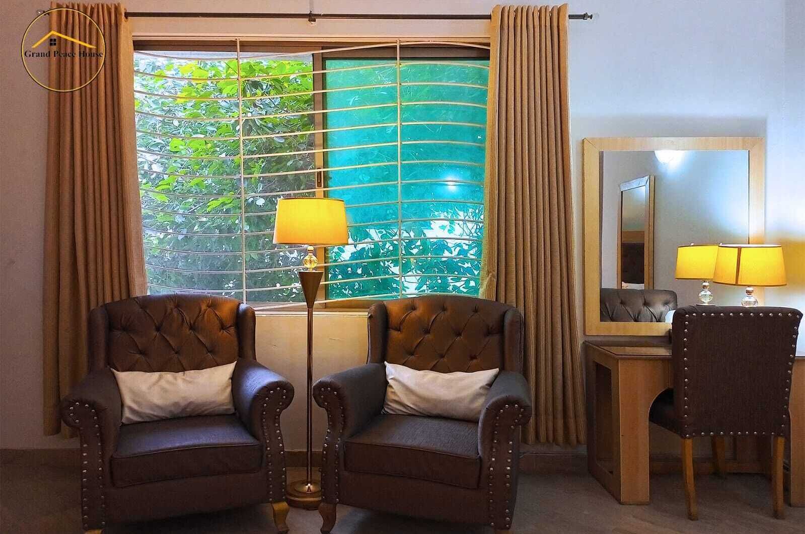 Um quarto com duas poltronas de couro, um abajur, uma mesinha de madeira e um espelho.