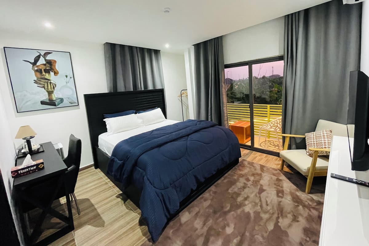 Quarto de hotel moderno com uma cama grande, uma escrivaninha, uma cadeira e uma varanda com vista.
