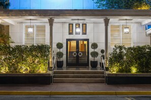 Entrada de hotel com portas duplas, duas plantas em vasos e um conjunto de degraus que levam à entrada.