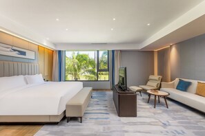 Quarto de hotel moderno com cama grande, sofá, escrivaninha e televisão.