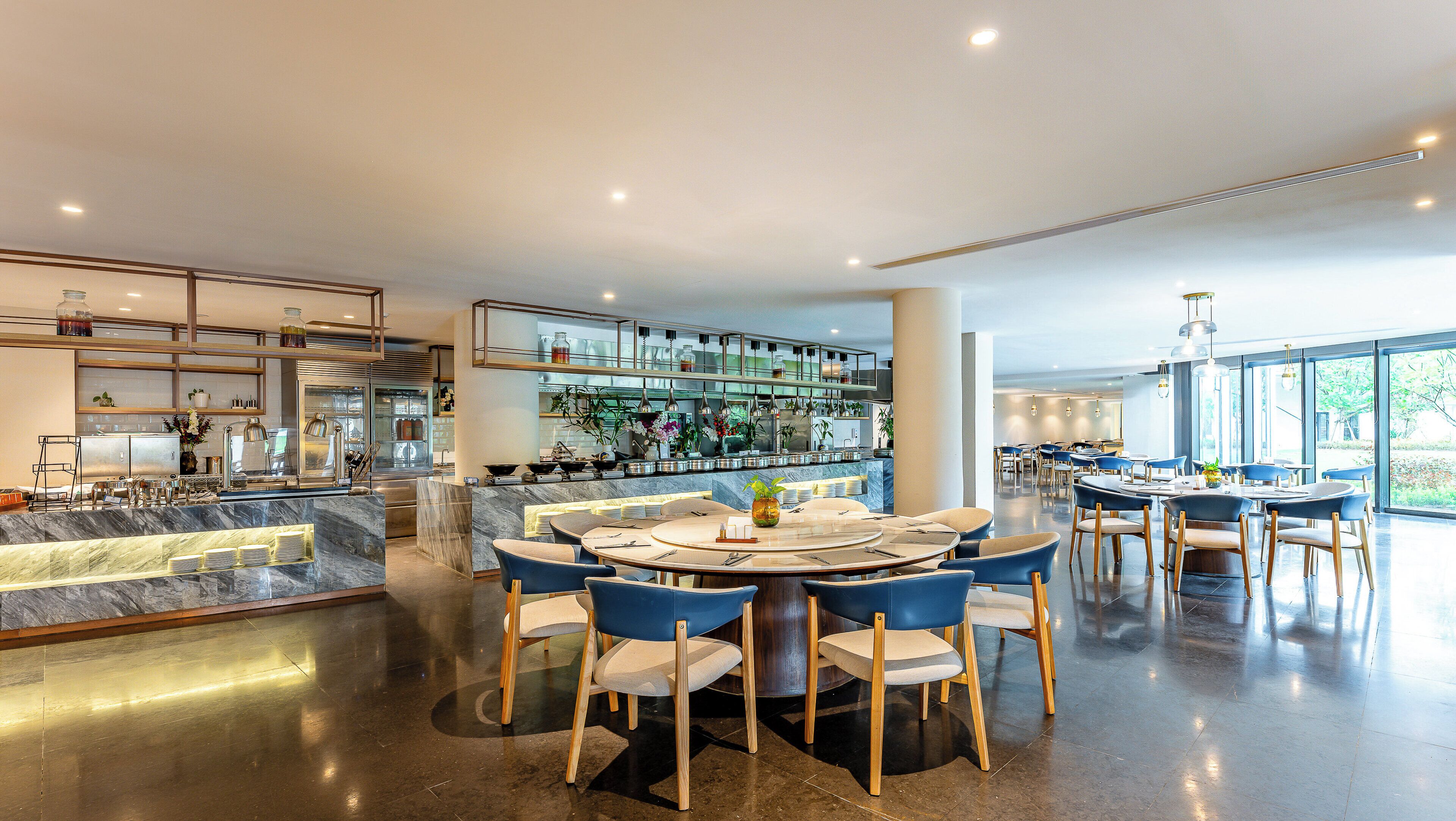 Uma sala de jantar moderna com um balcão de mármore, cadeiras azuis e uma mesa redonda central.