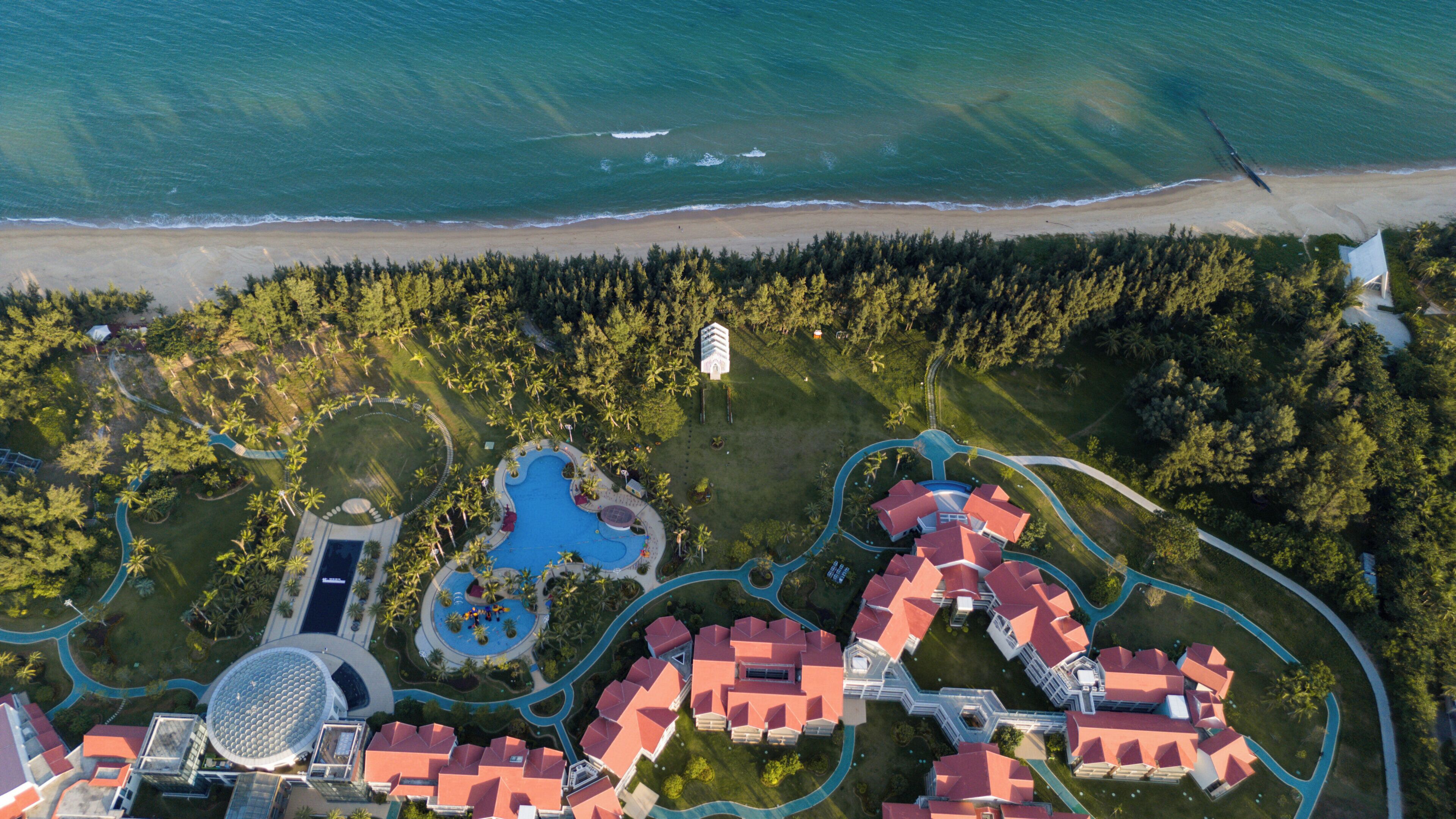Vista aérea de um resort com praia, piscina e vários edifícios.