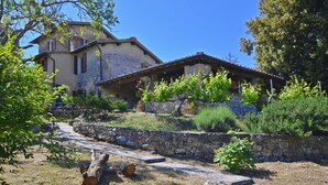 Uma casa rústica de pedra com um muro de pedra e uma escadaria de madeira que leva a uma porta de madeira.