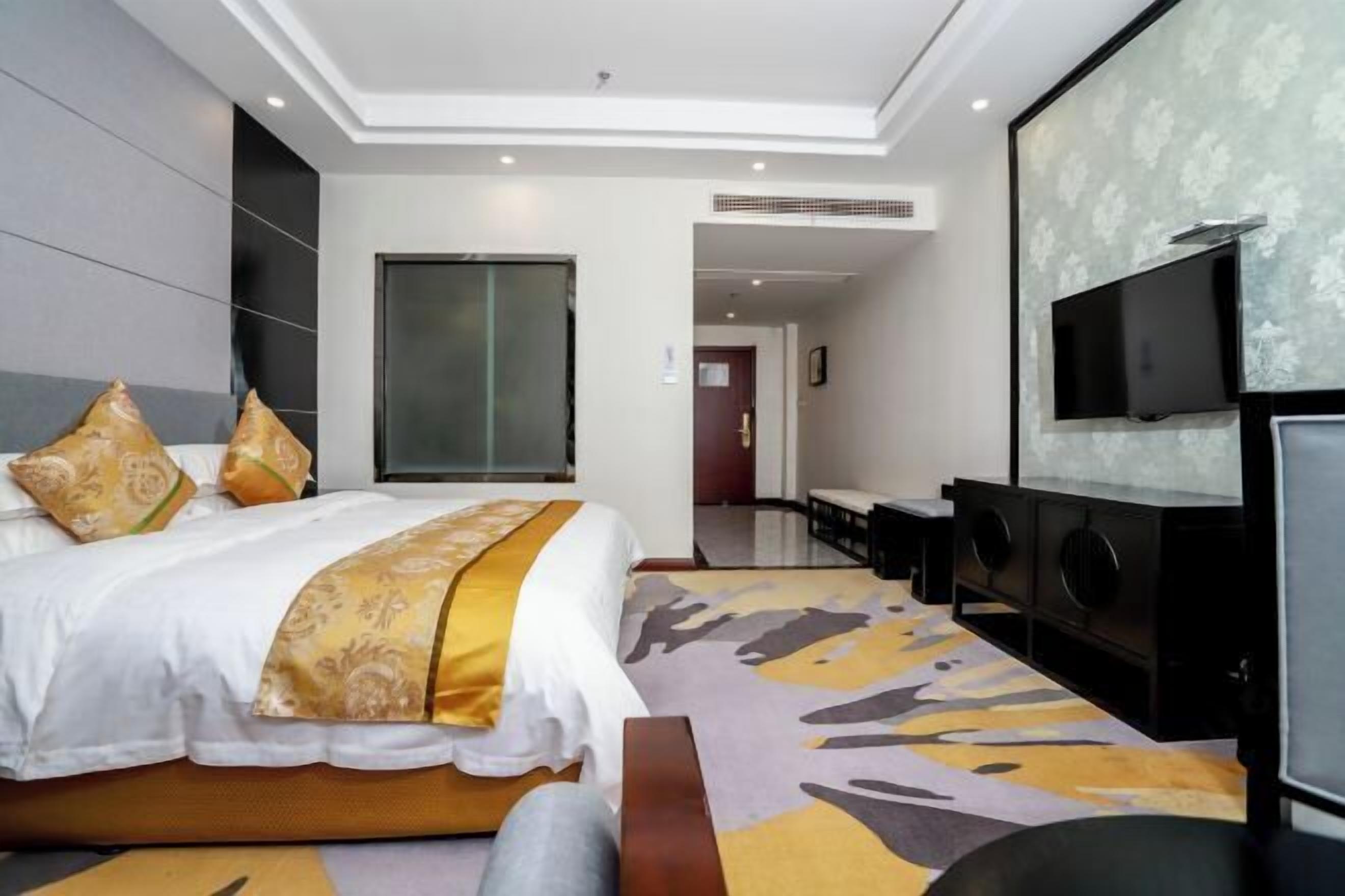 Quarto de hotel moderno com uma cama, televisão, escrivaninha e uma janela grande.