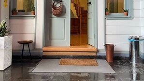 Entrada de casa com escada de madeira que leva ao interior, um tapete na porta e plantas em vasos.