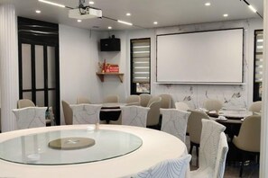 Sala de conferências com mesa redonda, cadeiras, projetor e quadro branco.