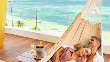 Um casal relaxando em uma rede em um deck de madeira, com vista para o oceano.