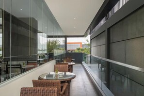 Varanda moderna com guarda-corpo de vidro, móveis de vime e vista para a cidade.