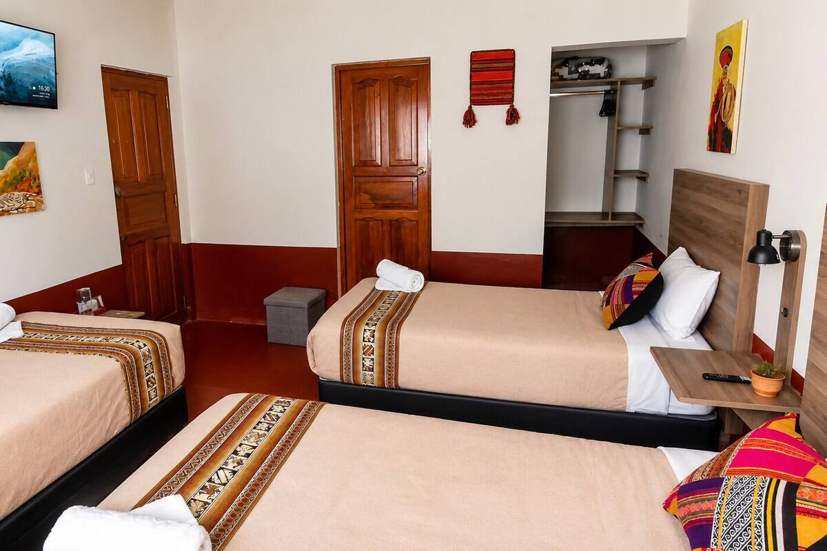 Quarto de hotel com duas camas, televisão, quadro, porta, mesa pequena e mesa de cabeceira.