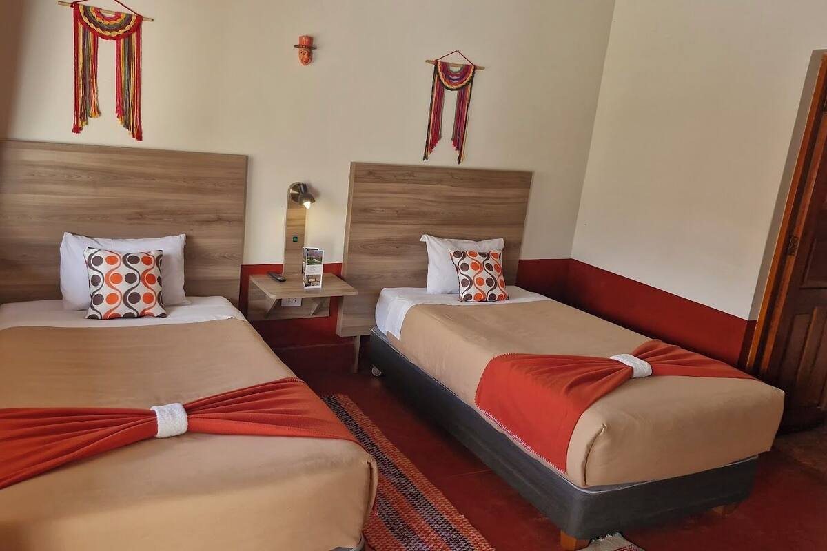 Quarto de hotel com duas camas, uma mesinha de cabeceira, um espelho e decorações nas paredes.