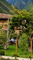 Uma pessoa sentada numa rede em um jardim exuberante, com montanhas ao fundo.