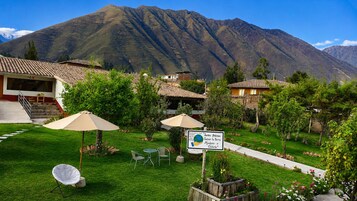 Um jardim exuberante com área de estar ao ar livre, uma placa que promove a consciência ambiental e montanhas ao fundo.
