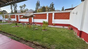 Um pátio com um edifício vermelho e branco, uma área de estar coberta e plantas em vasos.