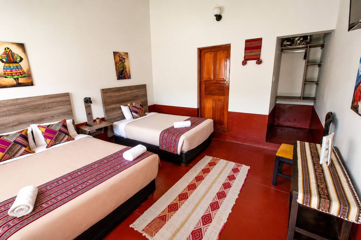 Quarto de hotel com duas camas, uma escrivaninha, uma cadeira, televisão e obras de arte nas paredes.