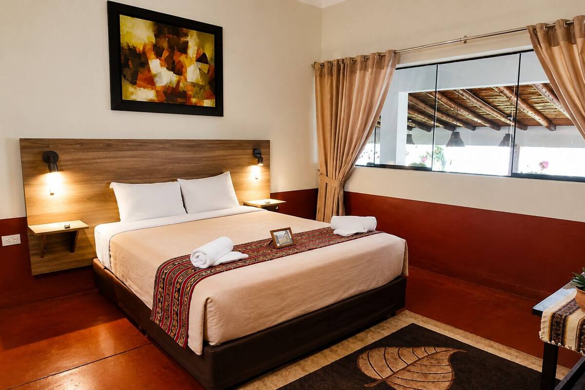 Quarto de hotel com uma cama, abajures, janela com cortinas, um quadro na parede e uma pequena mesa com uma planta.