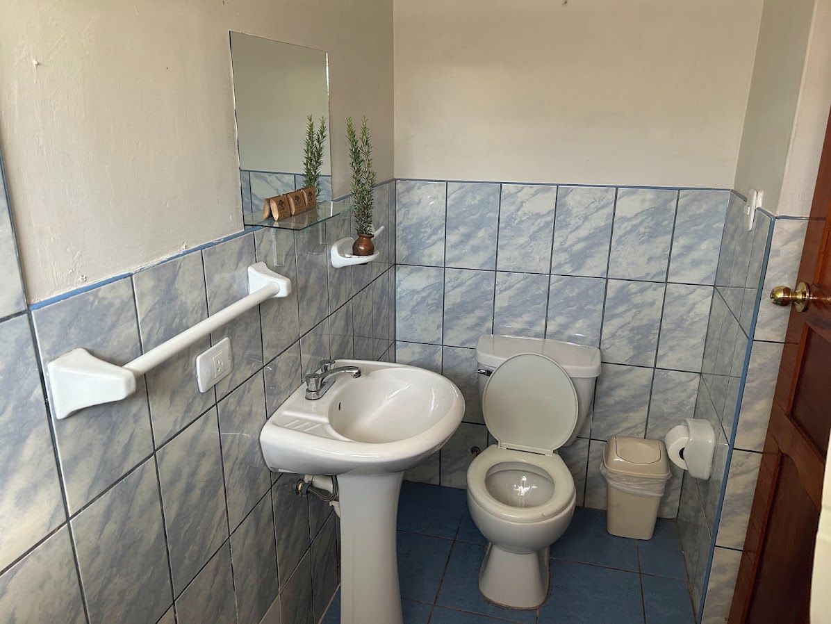 Casa de banho com lavatório branco, sanita e um contentor de lixo.