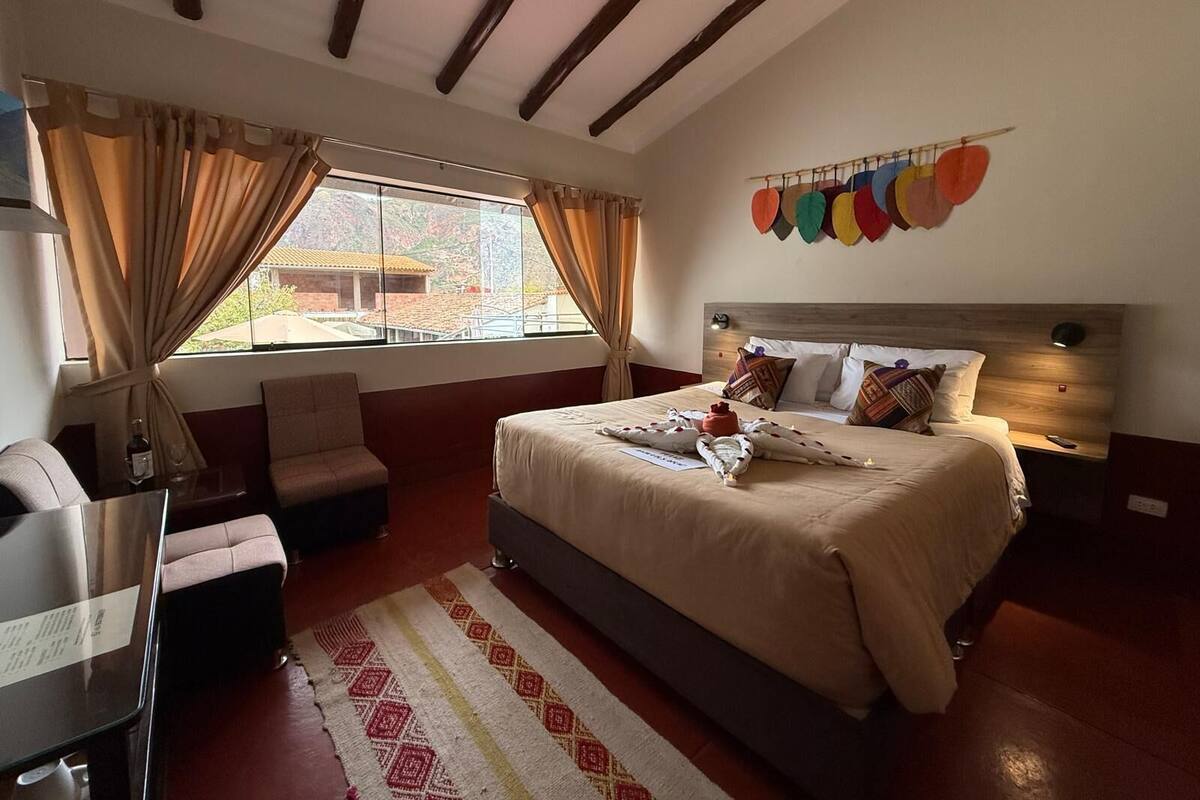 Quarto de hotel com cama, cadeira, escrivaninha e janela com cortinas.