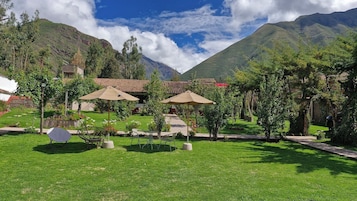 Um jardim exuberante com área de estar ao ar livre, um pequeno edifício com telhado em tijolos e montanhas ao fundo.