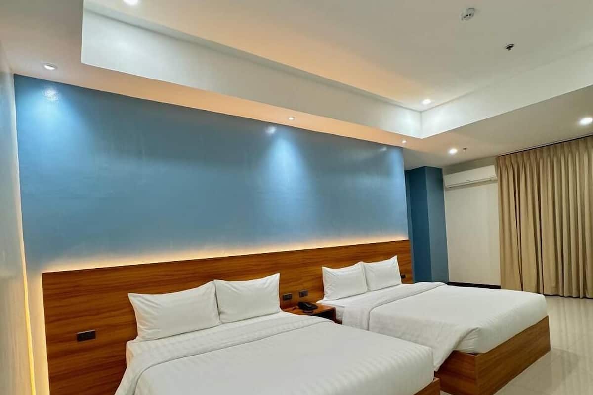 Quarto de hotel moderno com duas camas grandes, uma cabeceira de madeira e uma parede azul decorativa.