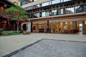 Um saguão de hotel com design moderno, apresentando uma grande janela circular, uma área de estar e um edifício de estilo tradicional ao fundo.