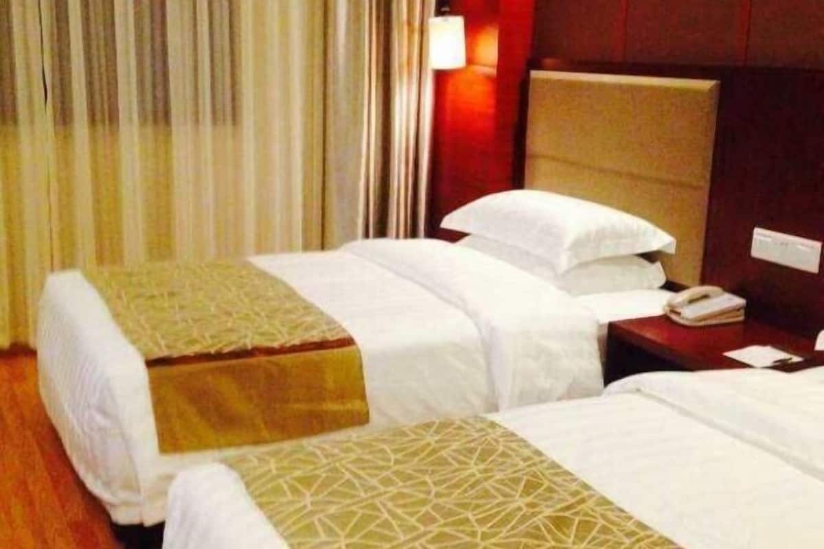 Quarto de hotel com duas camas, uma mesa de cabeceira com telefone e uma luminária na parede.