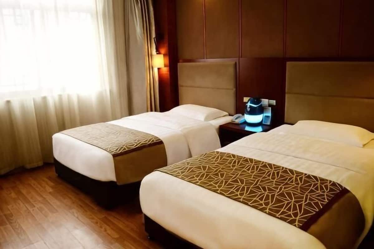 Quarto de hotel com duas camas, uma mesa de cabeceira com abajur e uma janela com cortinas.