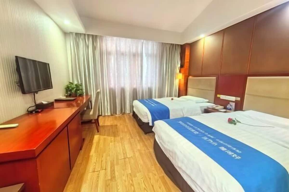 Quarto de hotel com duas camas, uma escrivaninha, uma televisão e uma janela com cortinas.