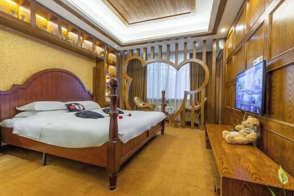 Quarto com cama de madeira, televisão, um banco e um painel decorativo na parede.